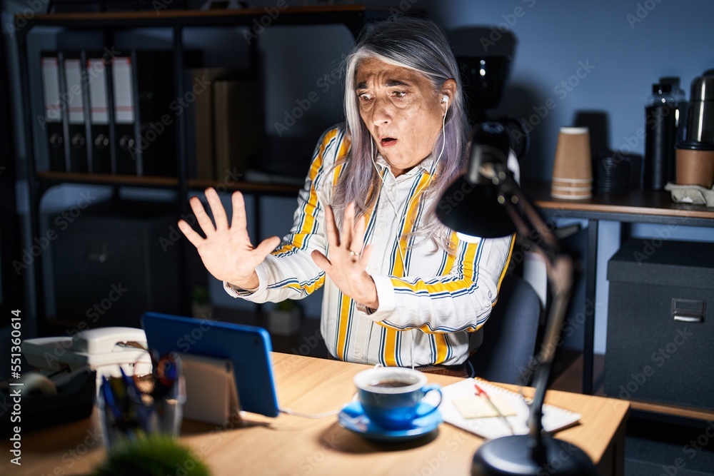 Middle age woman with grey hair working at the office at night afraid ...