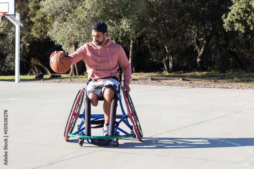 Bearded man in sports wheelchair dribbling streetball outside while ...