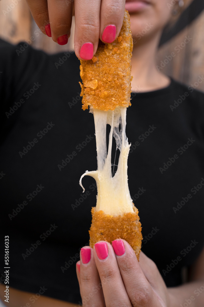 Foto de Woman stretching fried mozzarella cheese sticks. do Stock ...