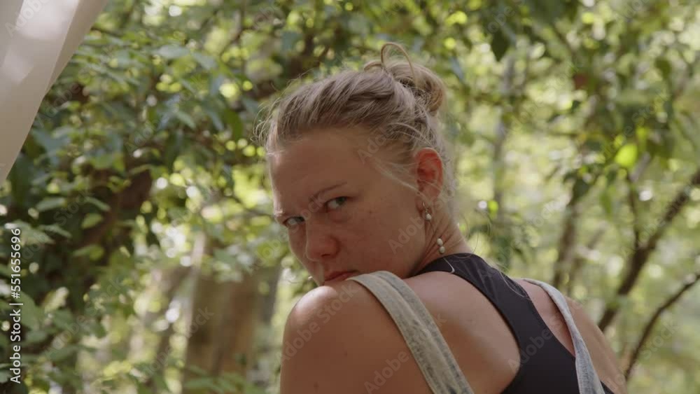 Cheerful blonde in nature turns around with smile and looks at camera ...
