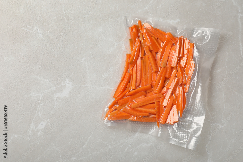 Vacuum packing with cut carrots on light grey marble table, top view ...