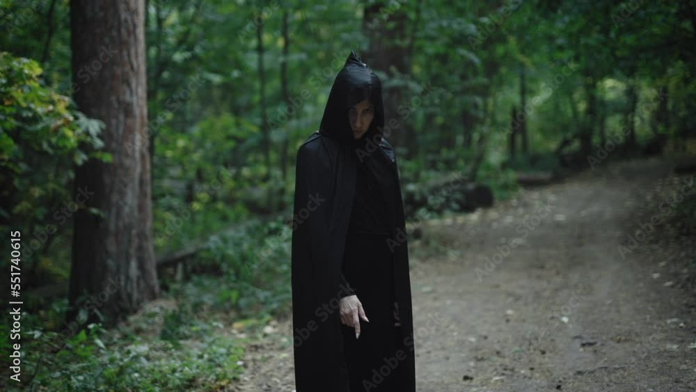 Frightening female witch in a mysterious forest. The witch points her ...