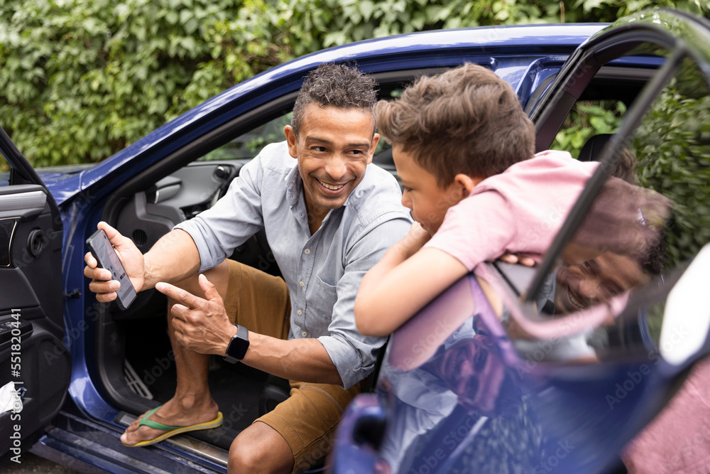 Excited father showing mobile phone to son leaning on car door Stock ...
