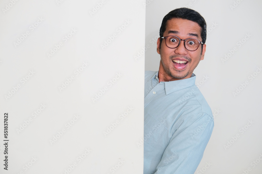 Adult Asian man hiding behind blank white billboard. Peeking out with ...