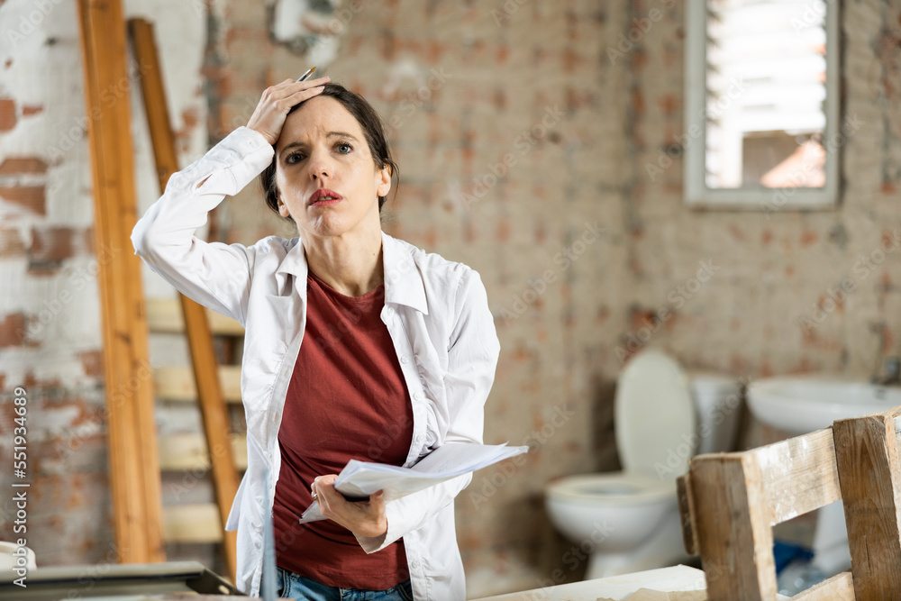 Confused woman standing in her apartment with papers in hands during ...