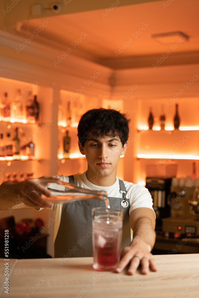 Bartender pouring tonic water in alcoholic cocktail in glass on bar ...