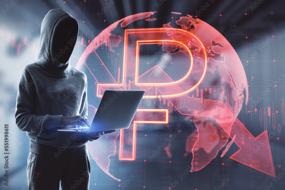 Hacker in hoodie using laptop with falling global red ruble arrow ...