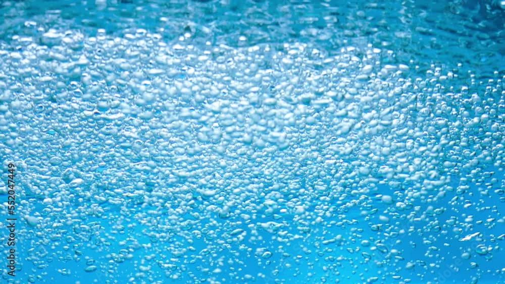 A stream of air bubbles rising onto the surface of blue water from the ...