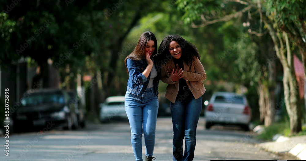Two beautiful diverse girlfriends walking and laughing together while ...