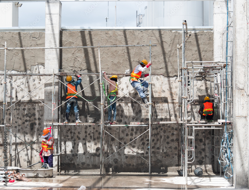 Construction workers standing on platform plastering concrete wall at a ...