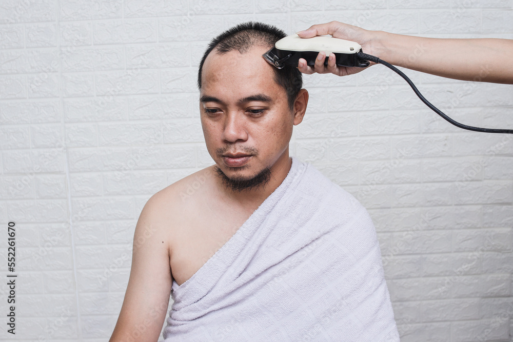 Muslim man wearing white ihram clothes doing Tahallul, shaving their ...