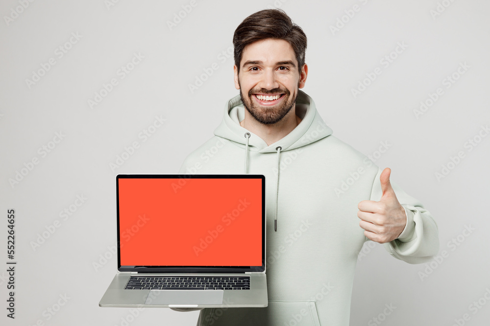 Young programmer man wear mint hoody hold use work on laptop pc computer with blank screen ...