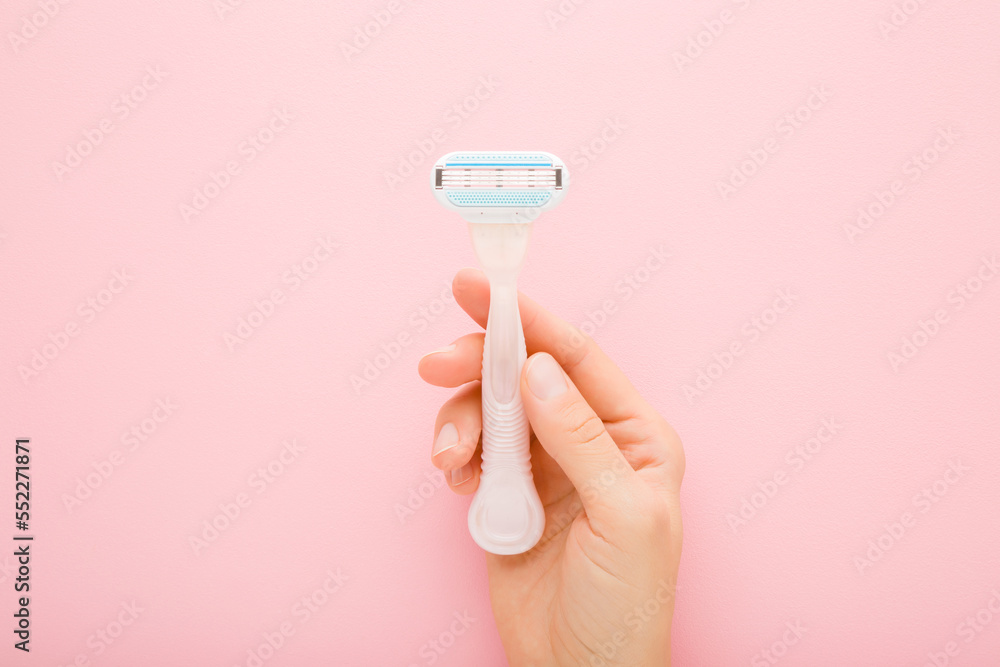 Young adult woman hand holding razor on light pink table background ...