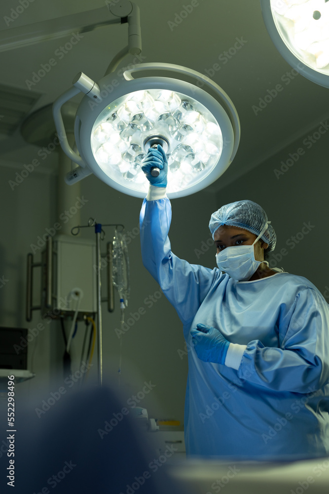 Vertical of biracial female surgical tech adjusting light in operating ...