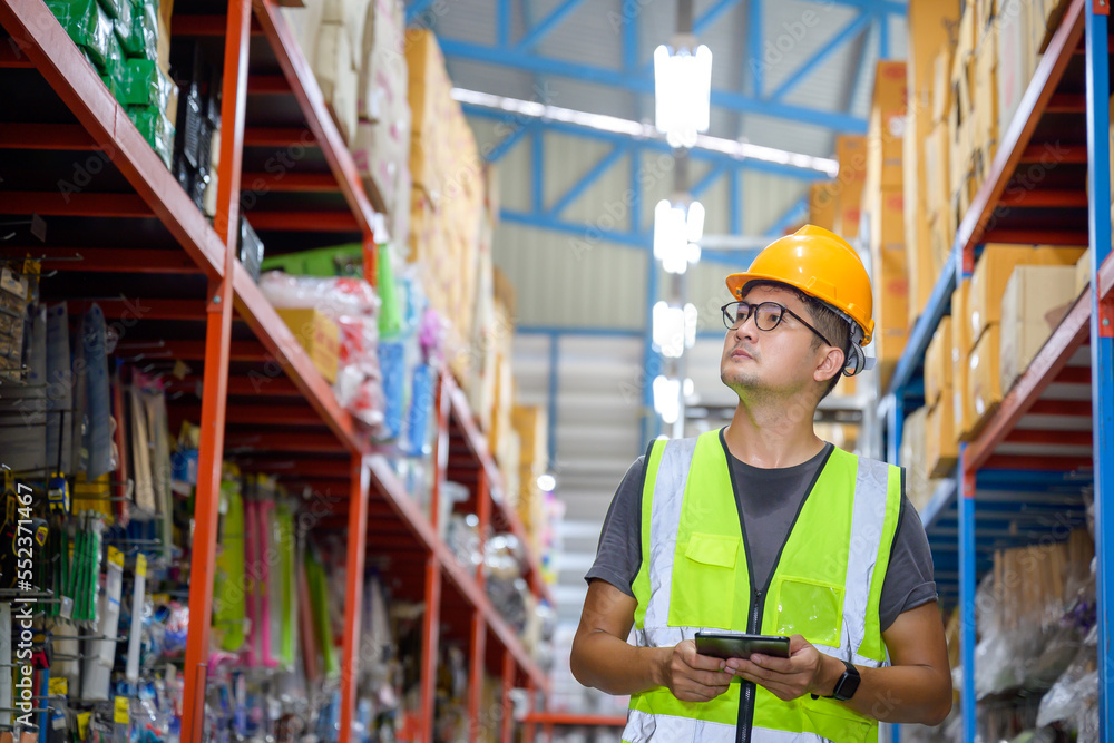 Asian male worker working inside a retail warehouse full of shelves ...