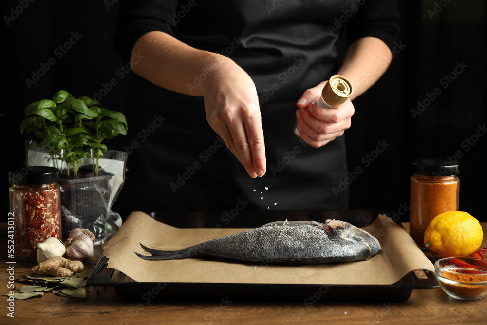 Salting food, the cook prepares fresh dorado on a black background ...