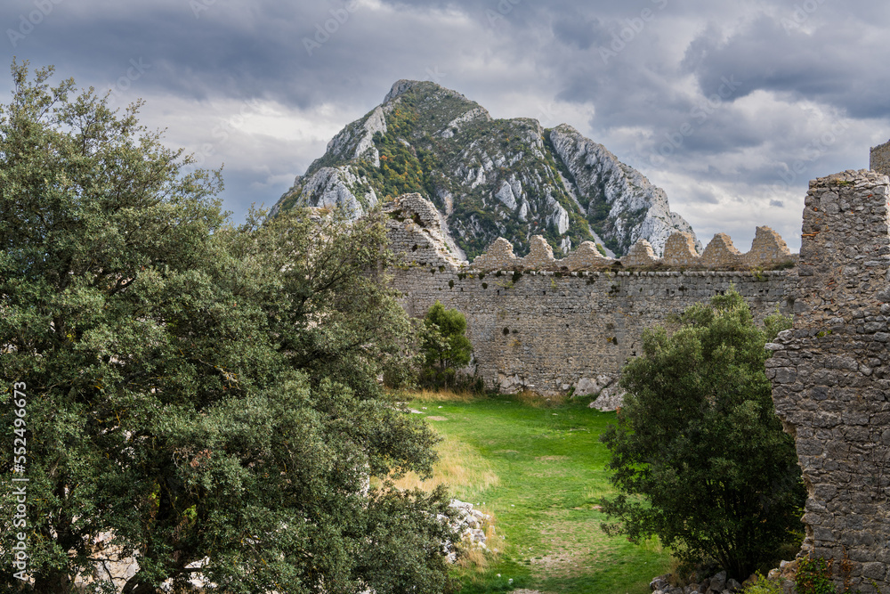 Castle wall and fortification below high mountain peak and dramatic ...