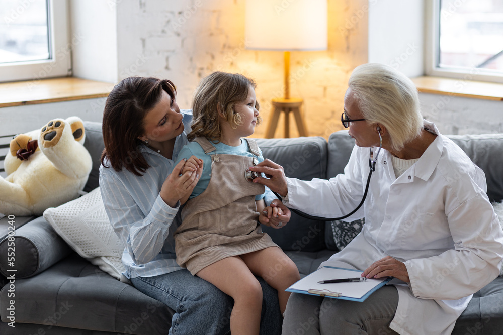 Kind female pediatrician doctor visiting his patient at home, examining ...