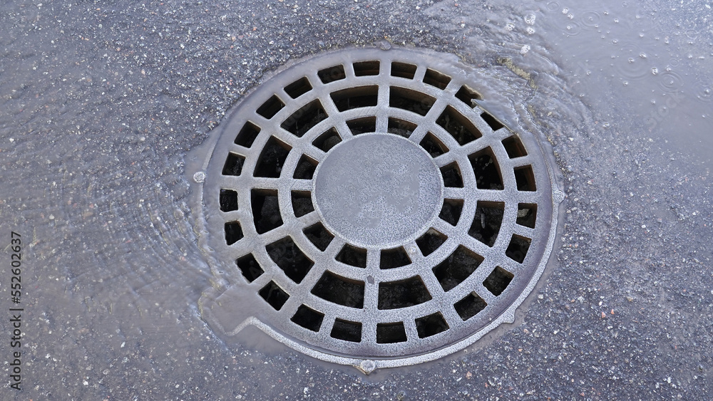 Water flows through the manhole cover, melting snow in the spring ...