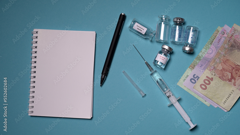 Blank notebook with pen on a blue background. Empty vaccine vials and a ...