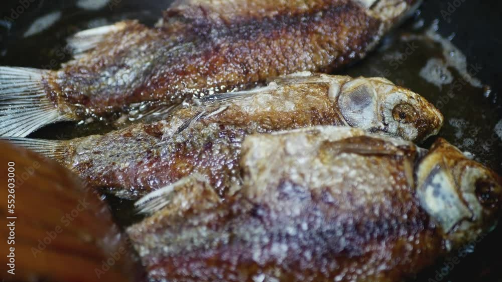 adding salt to freshwater fish with a crust in a frying pan, macro ...