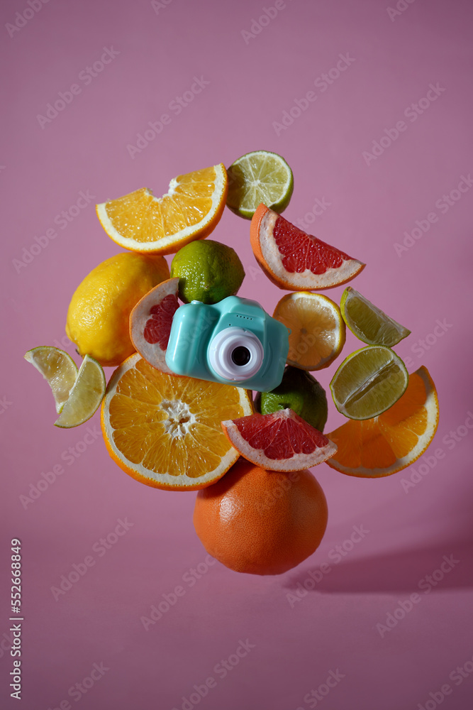 Whole and cut fruits and toy camera float in the air on a pink ...