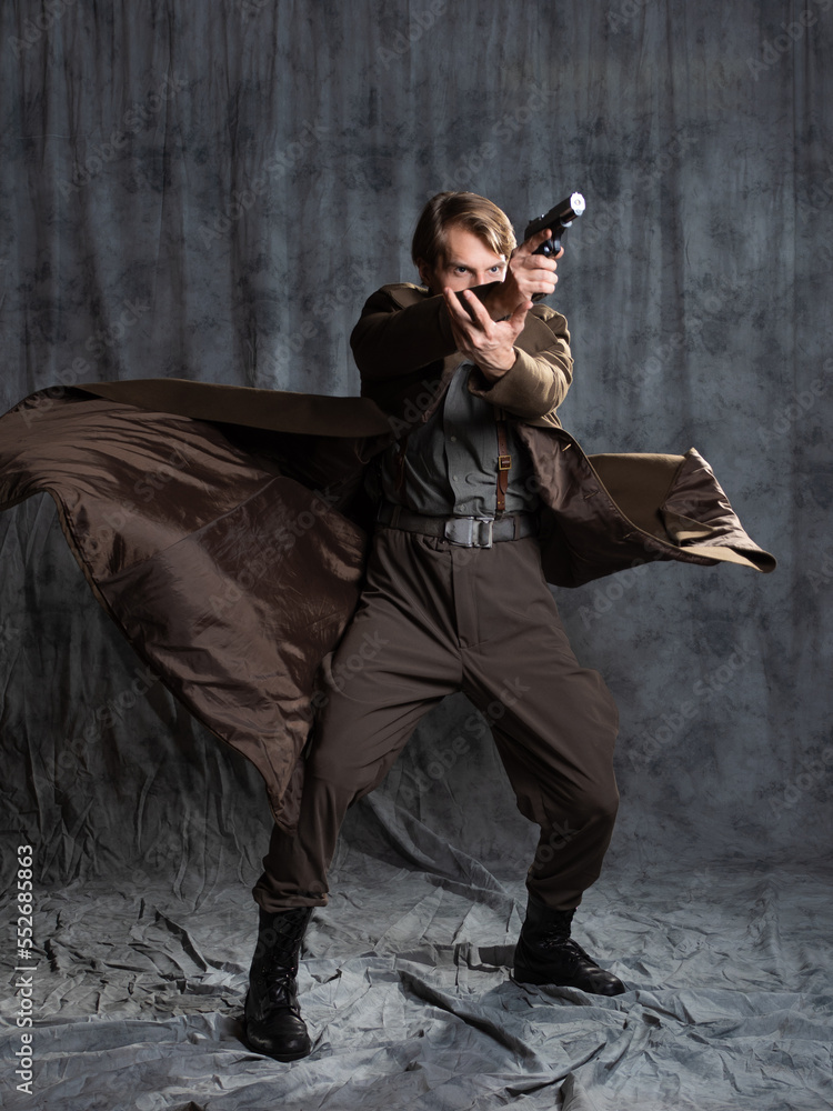 hero in a military style with a gun in his hands, a young man in a long ...