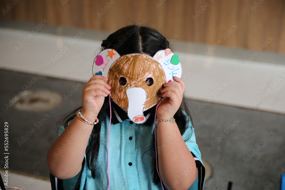 Little child girl wearing a coloured animal paper mask fronting her ...