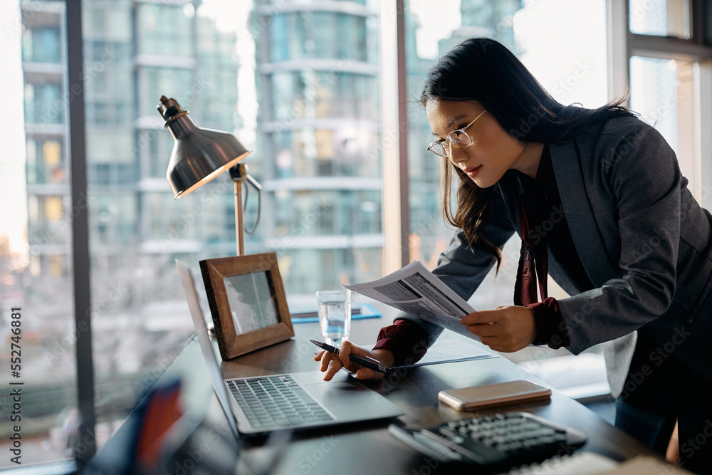 Asian female CEO working on laptop while analyzing business reports in ...