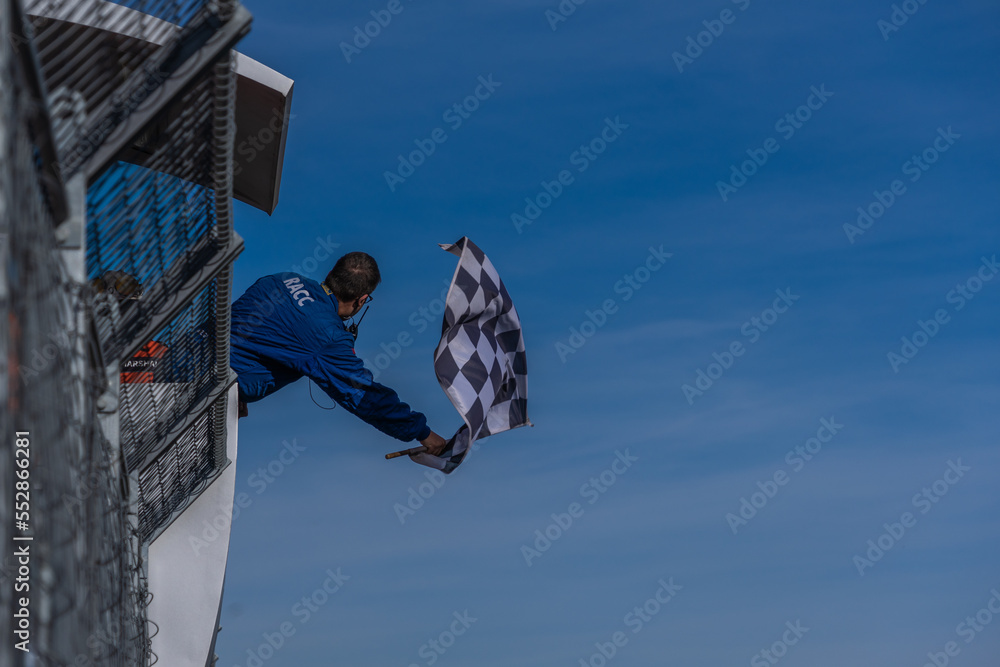 Man holding and waving checkered race flag at the finish line on a race track. Victory ...