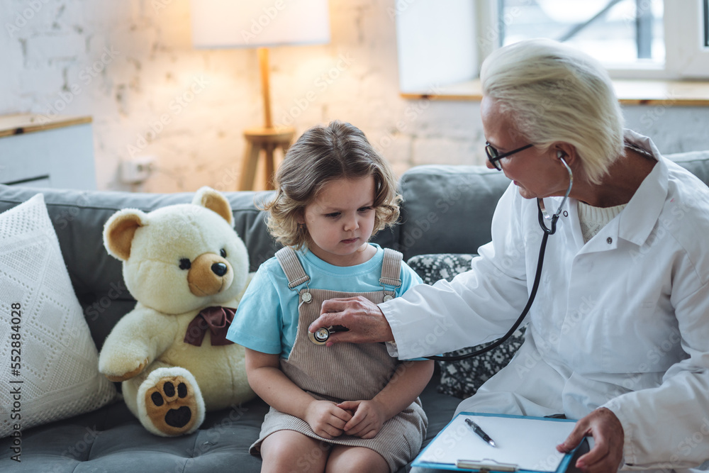 Kind female pediatrician doctor visiting his patient at home, examining ...