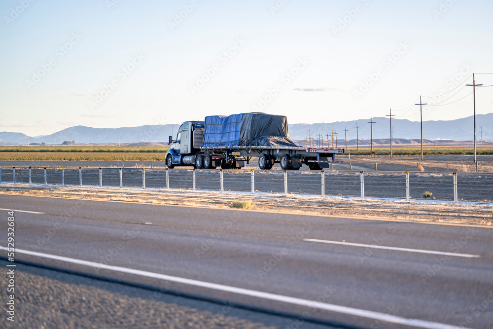 Low cab blue big rig long haul semi truck transporting covered by tarp ...