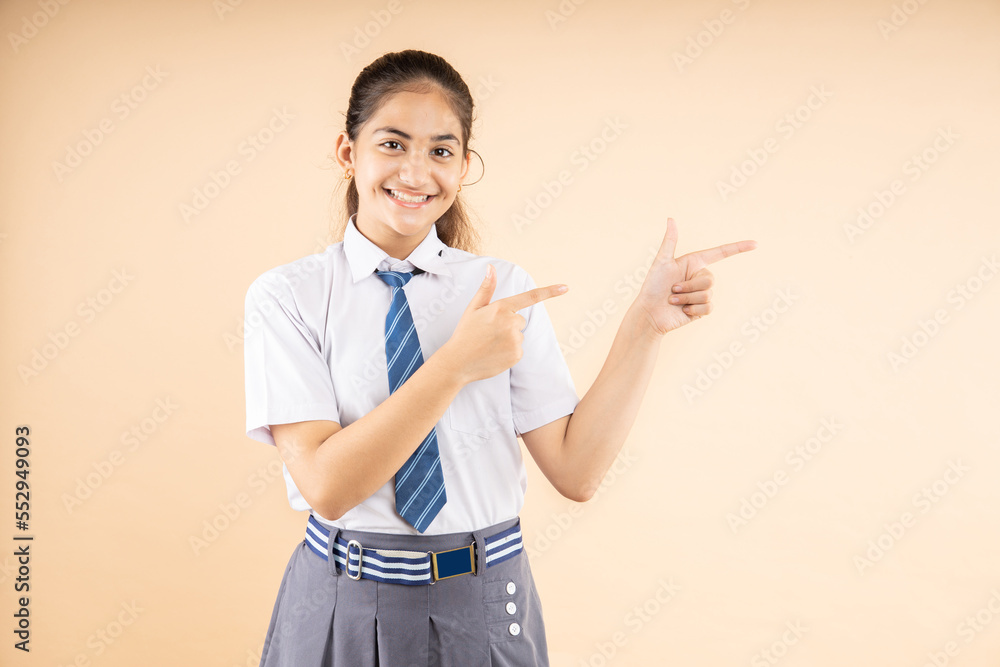 Happy Indian student schoolgirl wearing school uniform pointing at ...