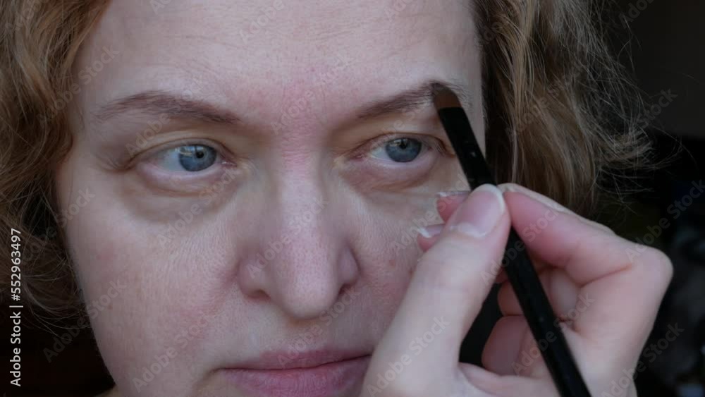 middle aged female's eye with drooping eyelid making eyebrow makeup ...