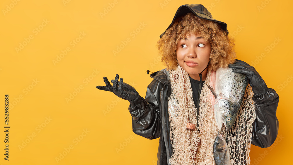 Confused curly haired female angler shrugs shoulders and looks aside ...