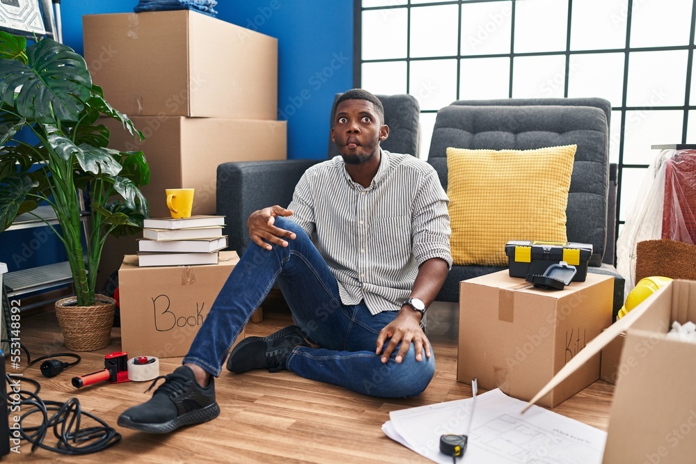 African american man sitting on the floor at new home making fish face ...