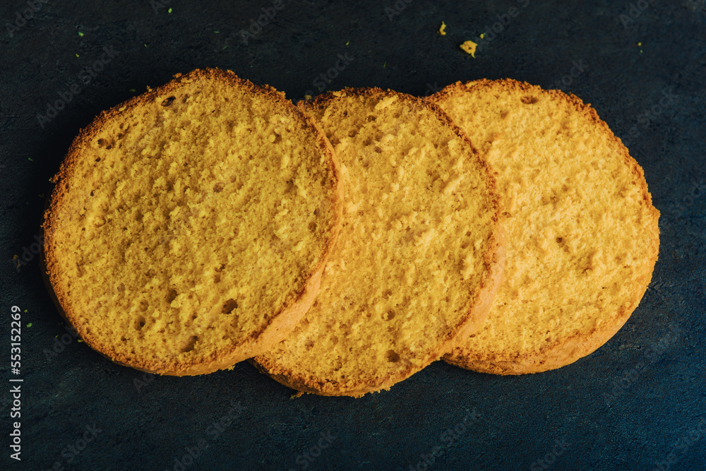 Three layers of a traditional sponge cake side by side on a dark ...