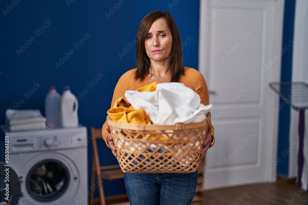 Middle age woman holding laundry basket at laundry room depressed and worry for distress, crying ...