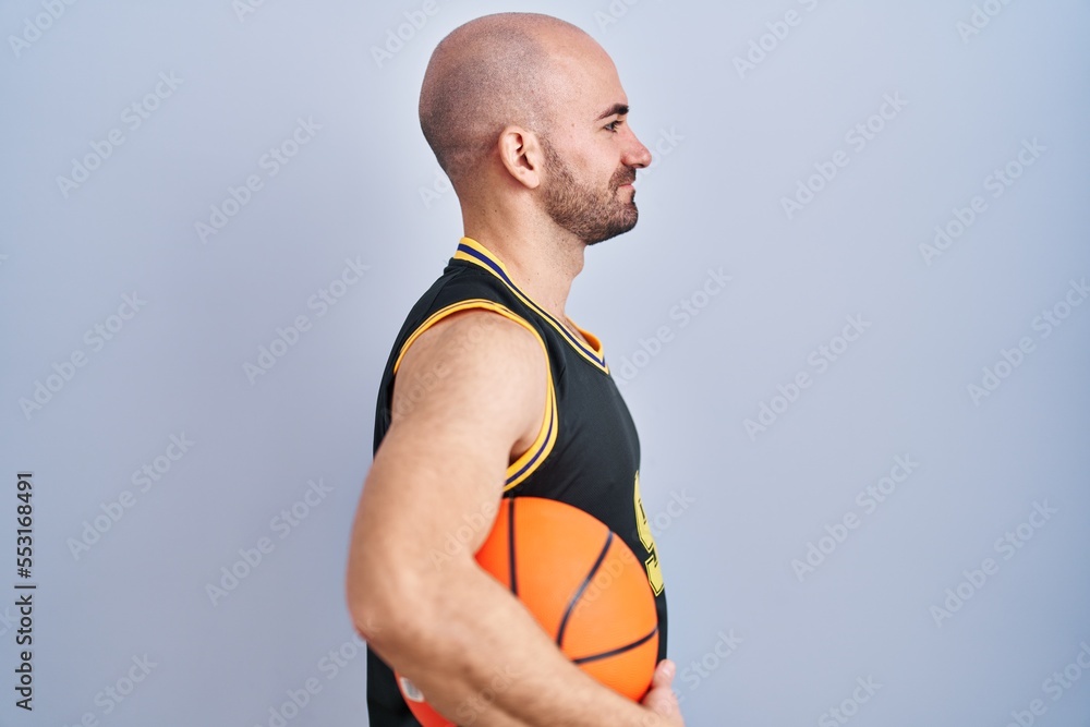 Young bald man with beard wearing basketball uniform holding ball ...
