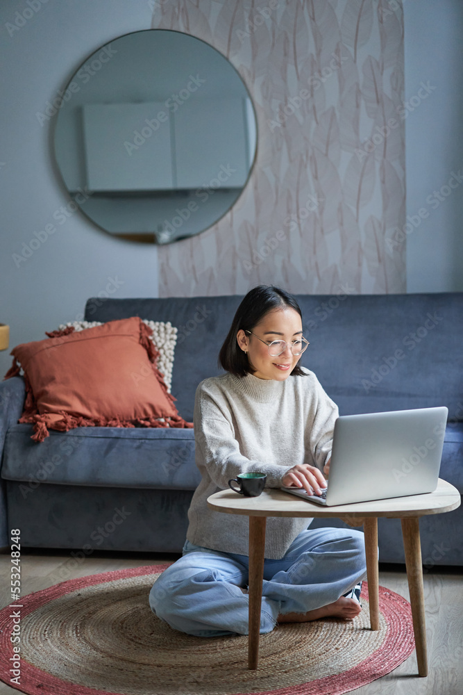 Vertical shot of korean working woman, sitting on floor at home with ...