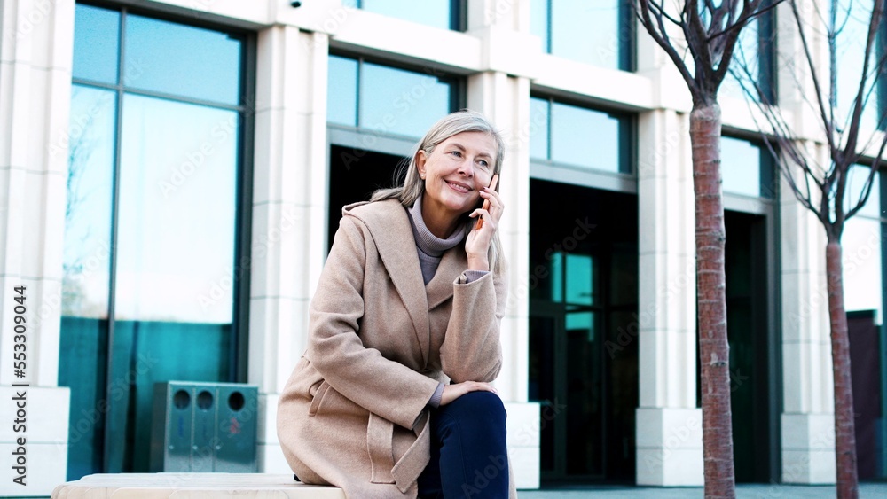 Senior beautiful happy grey-haired woman sitting outside talking on ...