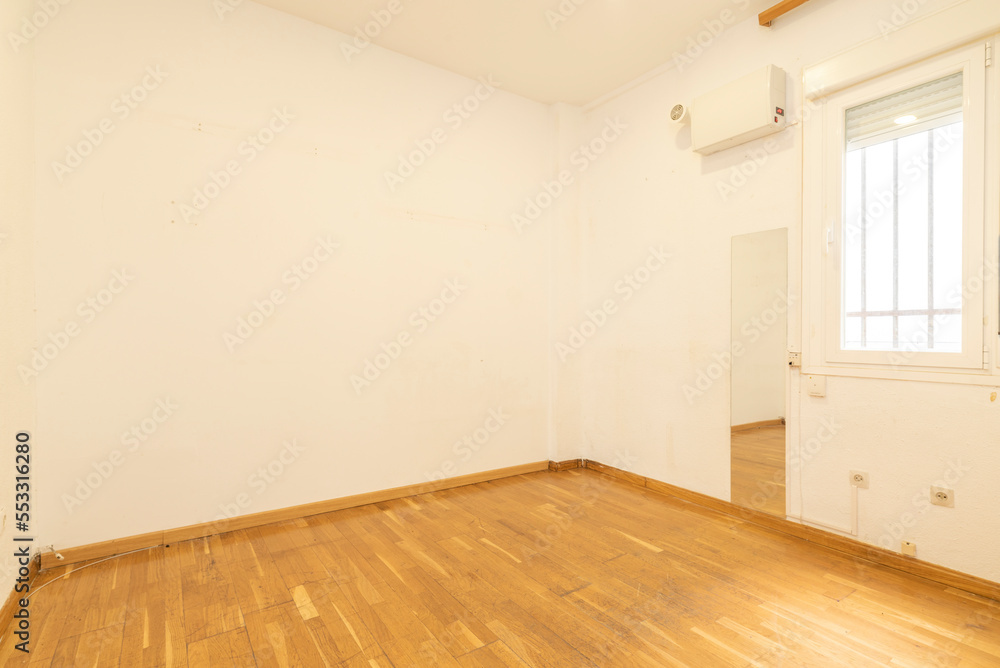 An empty room with a frameless mirror on the wall, worn wooden floors ...