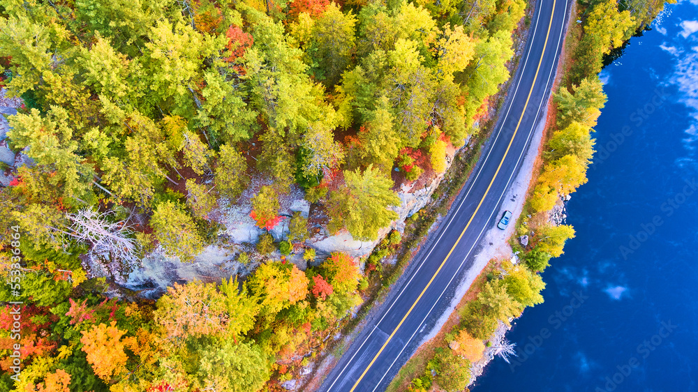 Aerial looking down on road next to lake and surrounded by fall foliage ...
