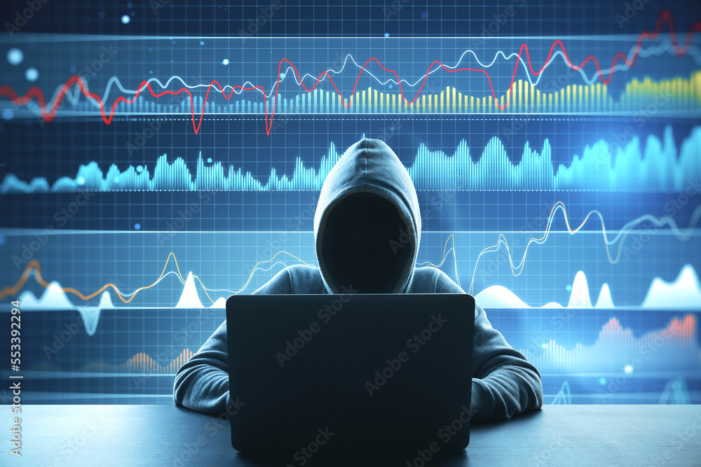 Hacker at desktop using laptop computer with digital business graph ...