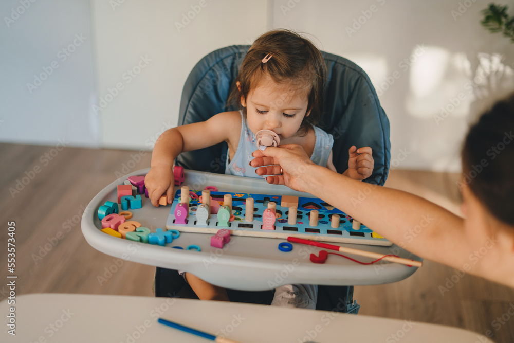 Baby girl sitting on high-chair doing educational logic toys for kids ...