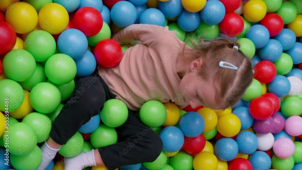 Cute little girl playing on multi coloured plastic balls in big dry ...