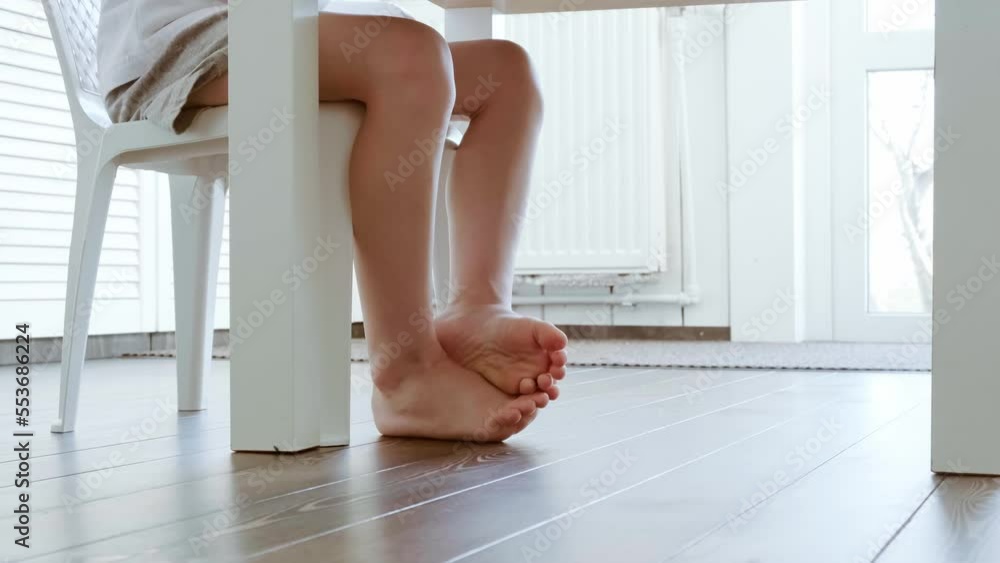 The moving barefoot legs of child sitting at the table. Concept of a ...
