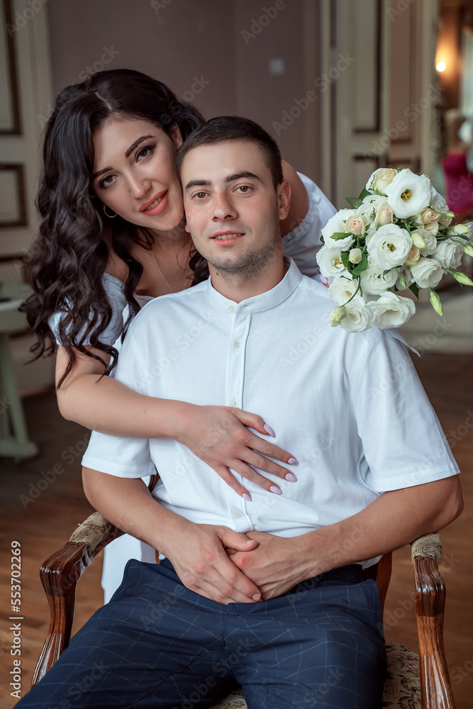 The bride passionately embraces the groom. The groom sits on a chair ...