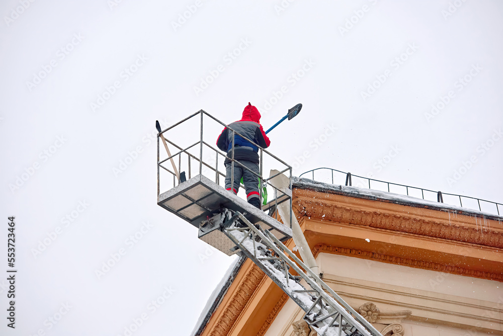 Foto de Man on lift crane remove icicles and snow from roof. Man with ...