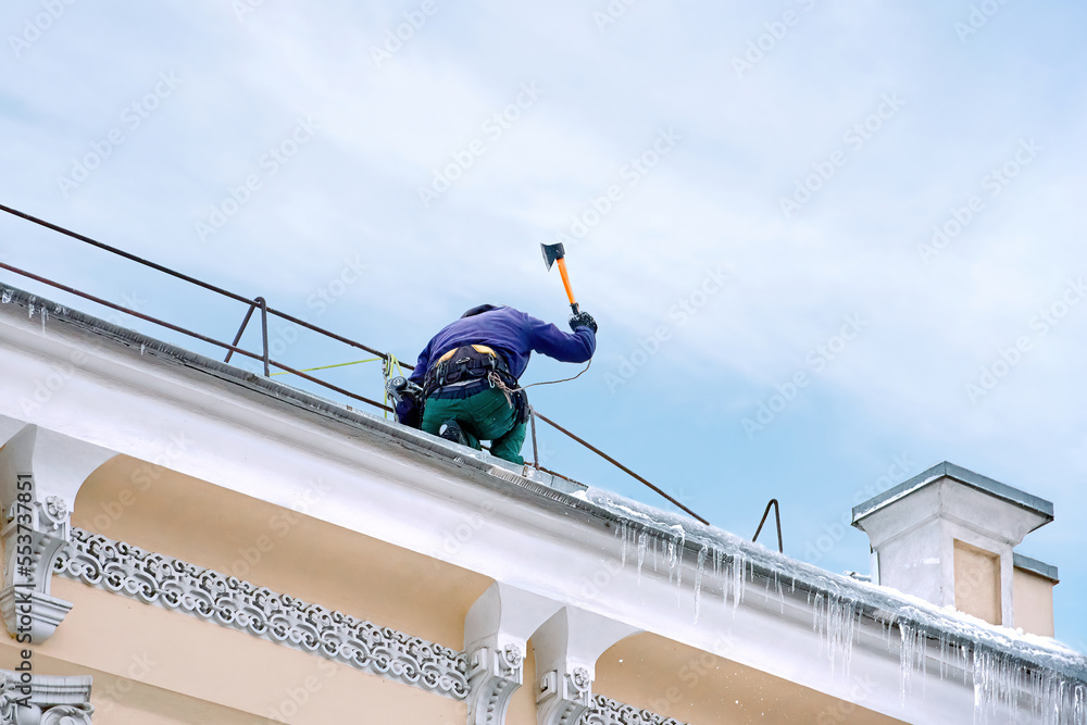 Worker on roof breakin ice and icicles with axe. Industrial alpinist ...